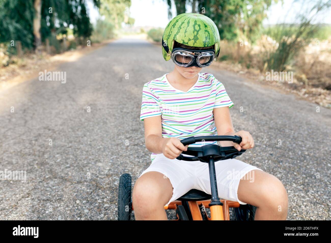 Serious kid in trendy wear and goggles riding go kart with pedals on ...