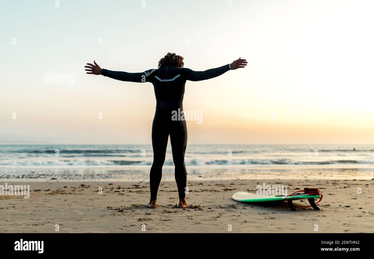 Full body back view of unrecognizable surfer in black wetsuit standing ...
