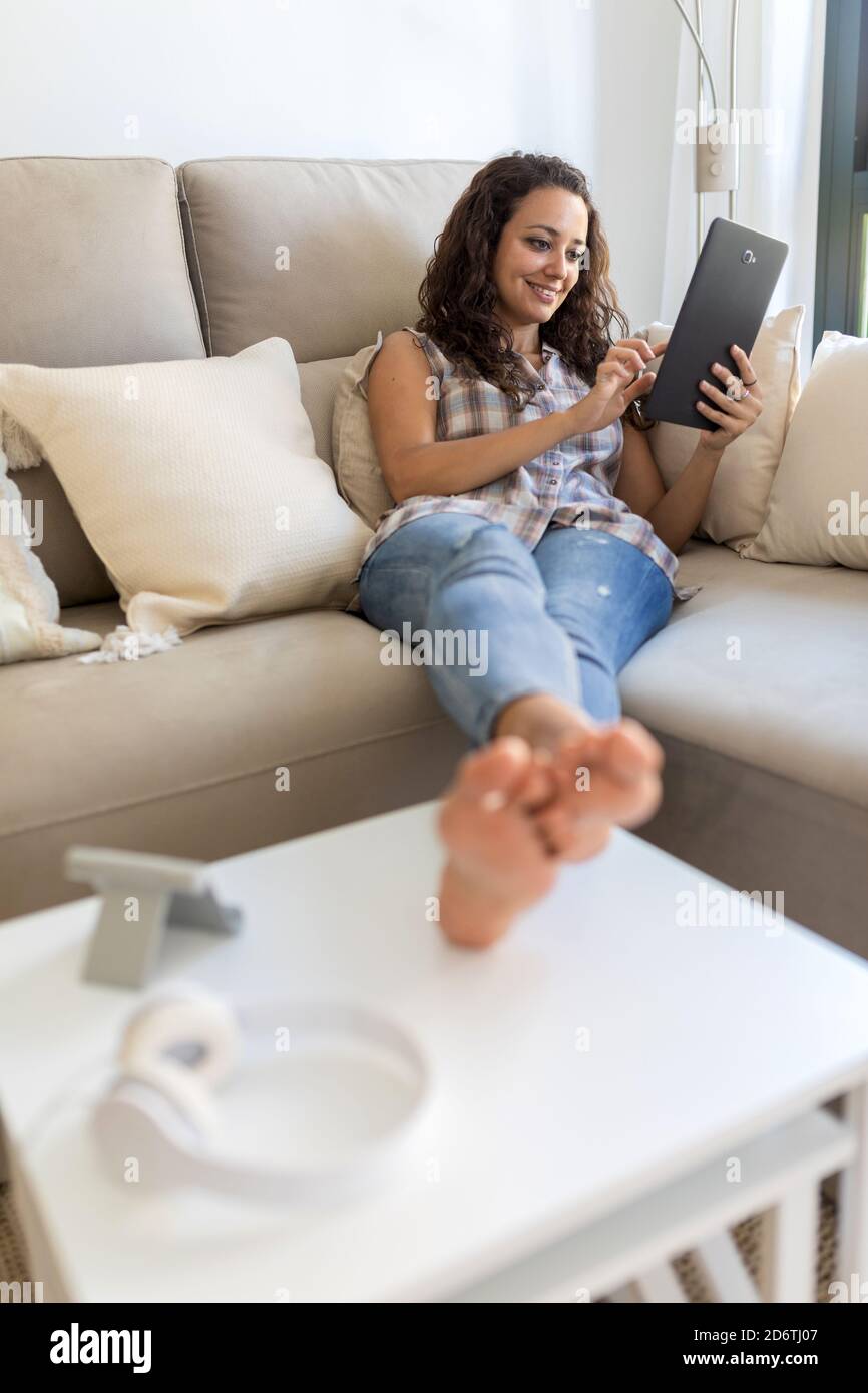 Positive female wearing domestic clothes sitting on soft couch at home ...
