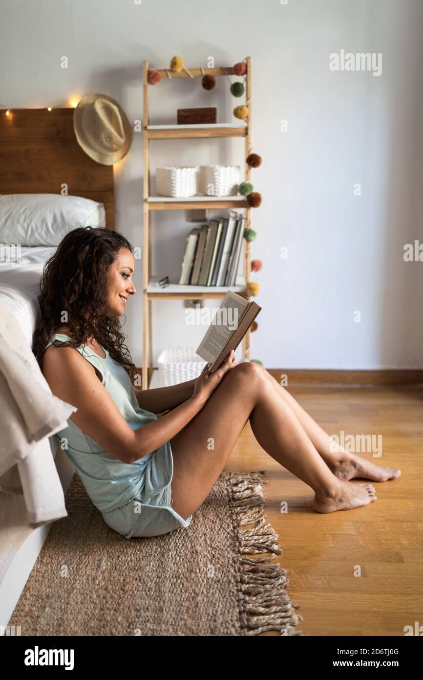 Side view of gentle female in pajamas sitting on floor near bed and ...