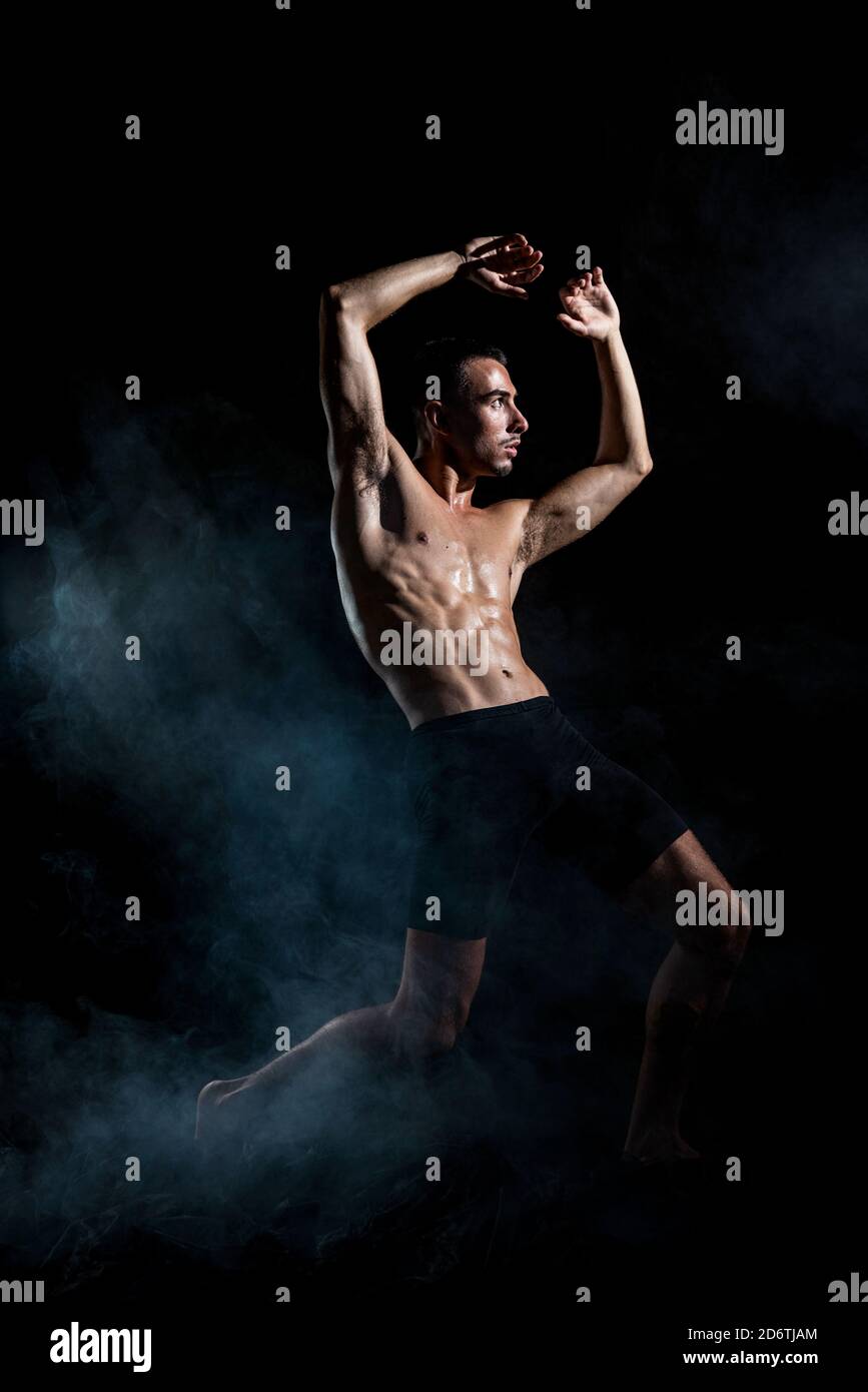 Full body of faceless tanned sporty shirtless dancer in shorts raising ...
