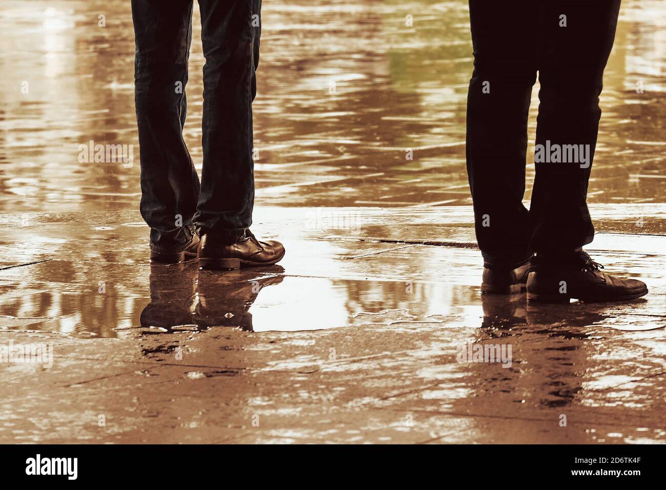 Feet of people standing in the rain. Men wait out a sudden downpour ...