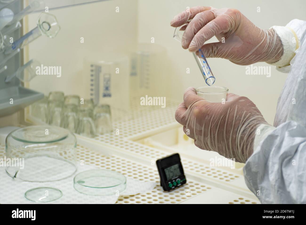 Scientist in protective white coat, mask and gloves analyzes a virus or ...