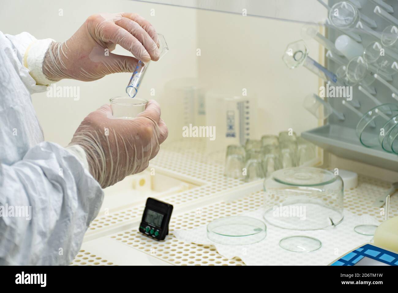 Scientist in protective white coat, mask and gloves analyzes a virus or ...