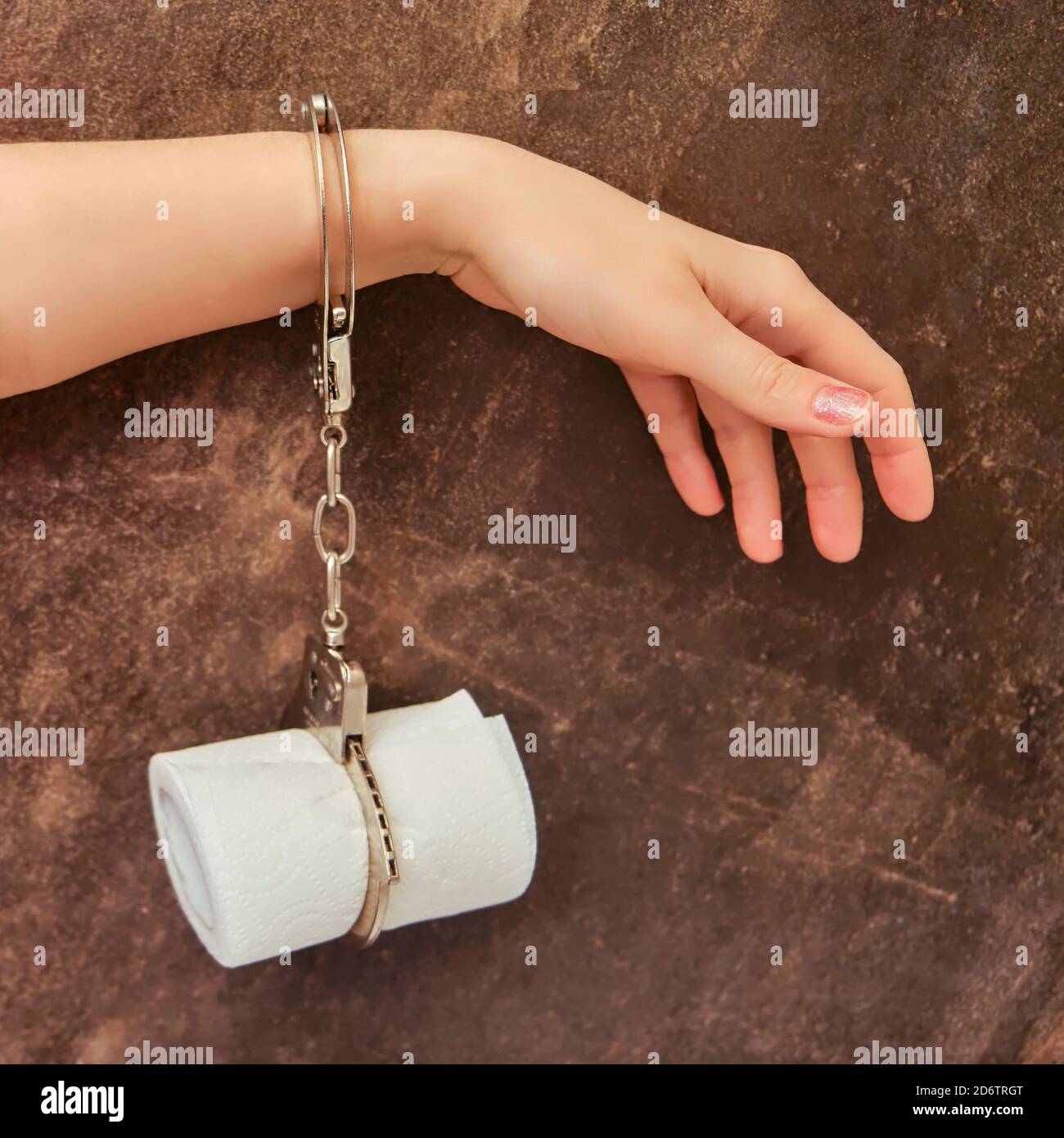 A woman's hand is handcuffed to toilet paper, a background of dark ...