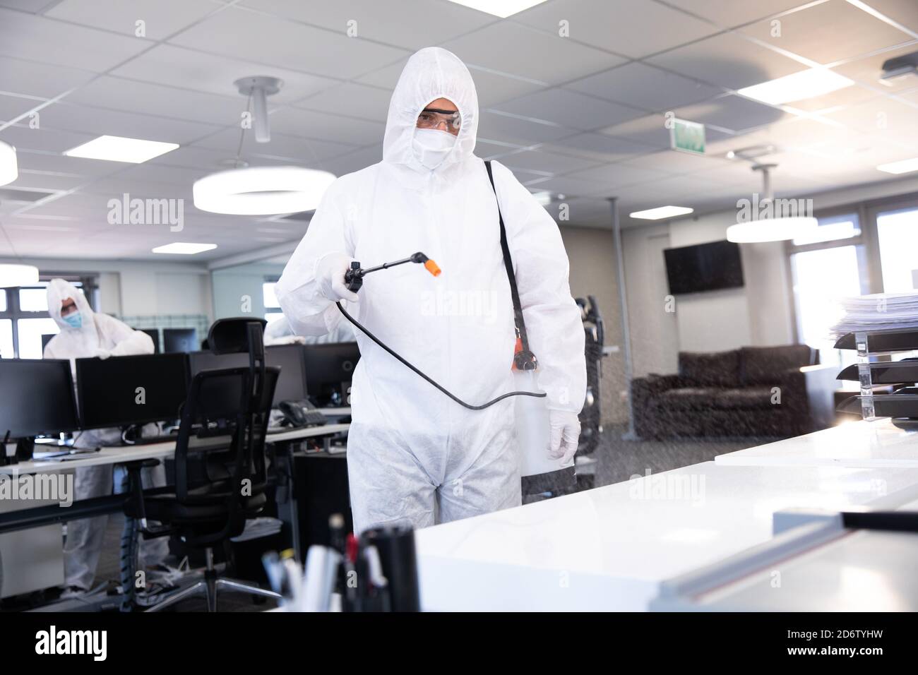Worker wearing protective suit, face mask and gloves sanitizing office ...