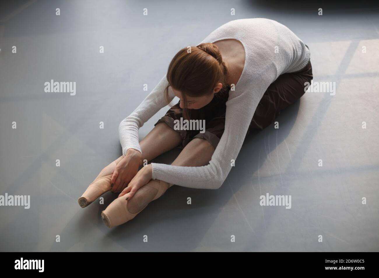 young ballerina in rehearsal wear stretching legs in choreography class ...
