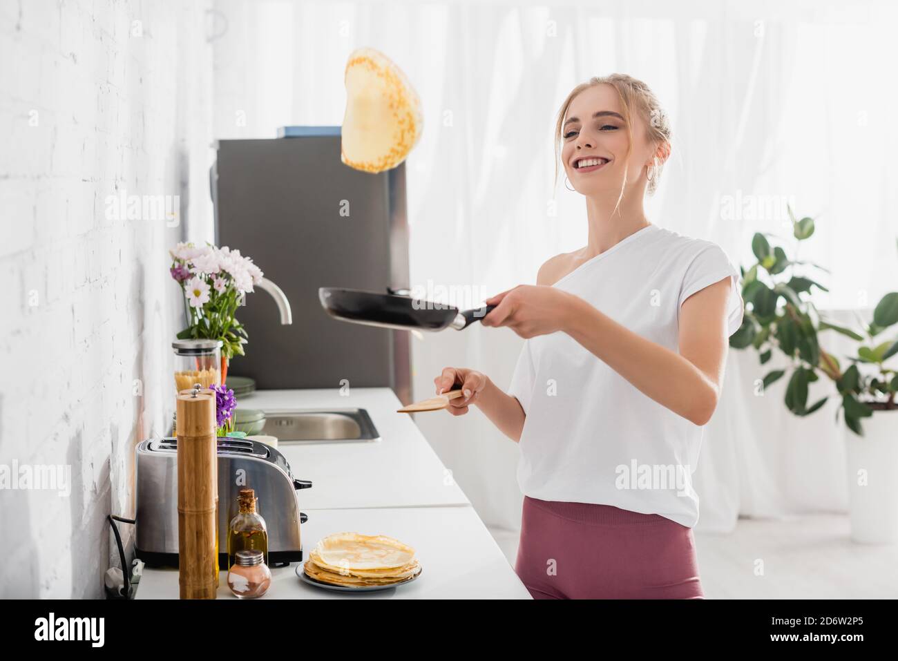 joyful young woman in white t-shirt throwing up pancakes on frying pan ...