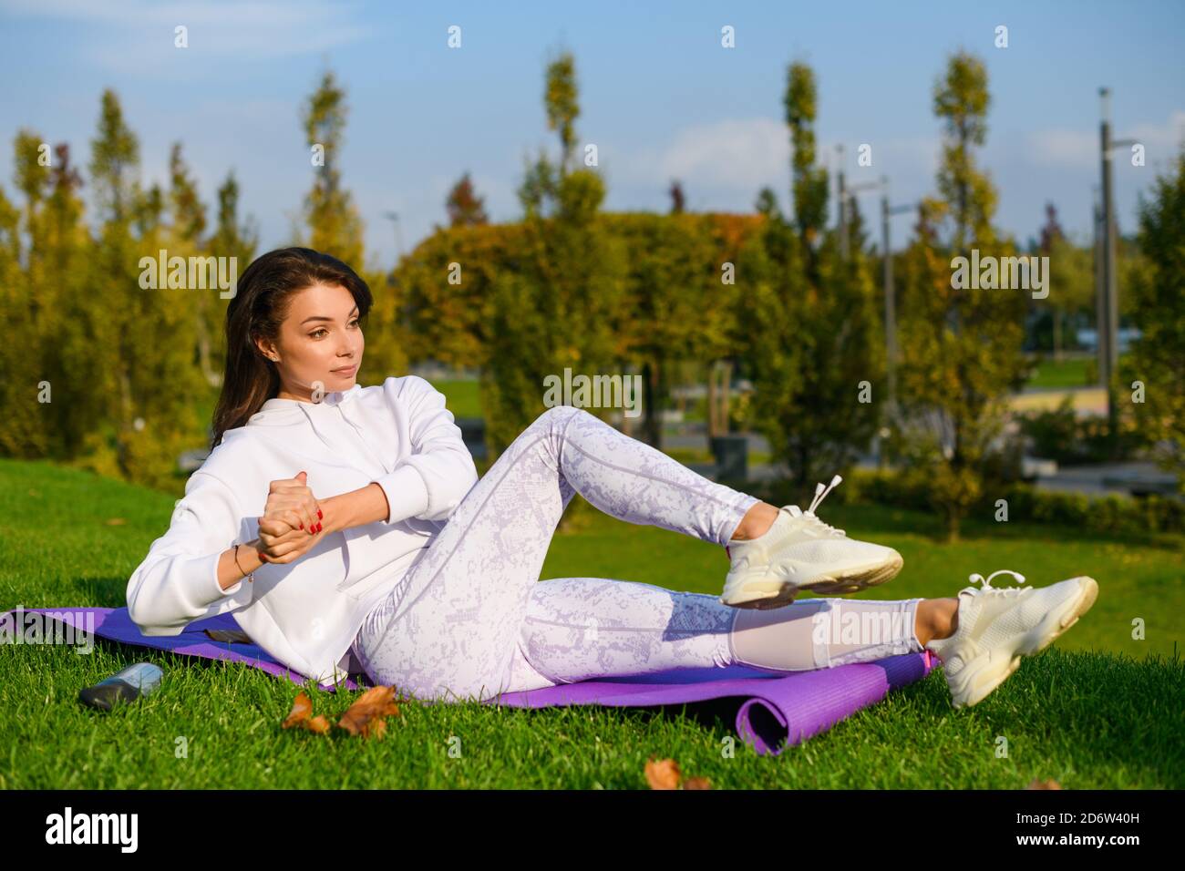 Pretty brunette sporty woman lay on mat at sunny green day and make ...