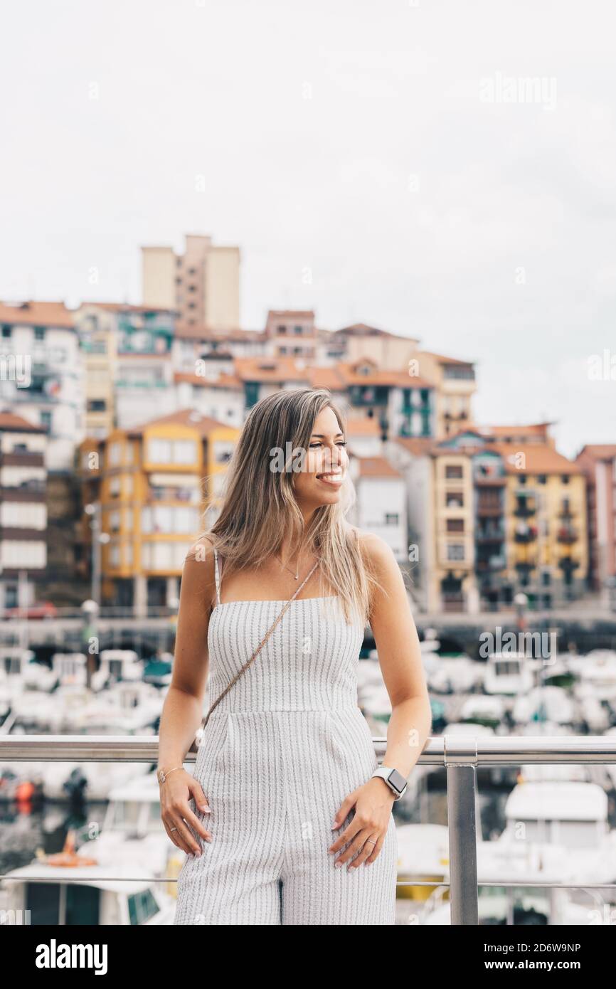 Young woman leaning against a railing, with a port and a small village ...