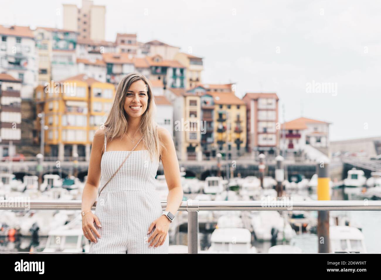 Young woman leaning against a railing, with a port and a small village ...