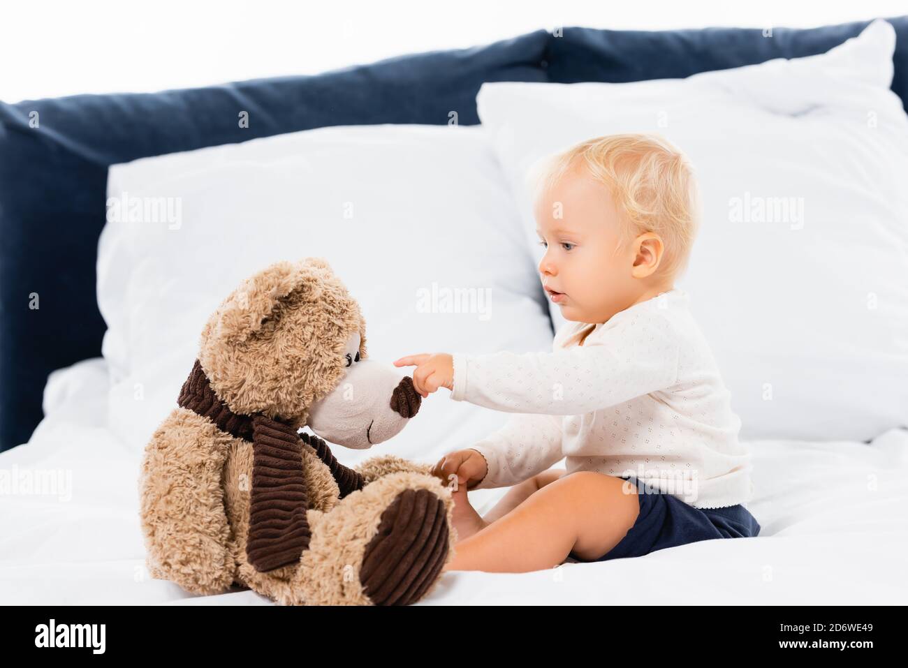 Toddler boy pointing at soft toy on bed on white background Stock Photo ...