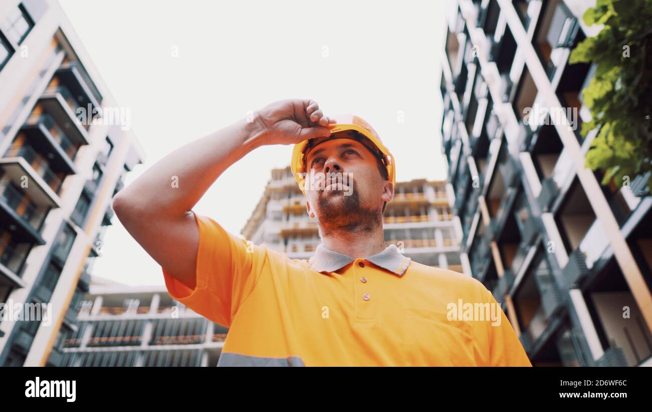 Serious Caucasian builder stands at construction site puts on orange ...