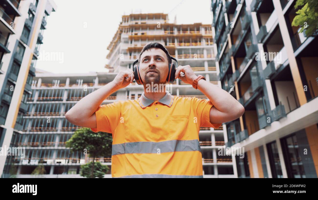 Builder covers his ears, ear muff to protect workers ears. Construction ...