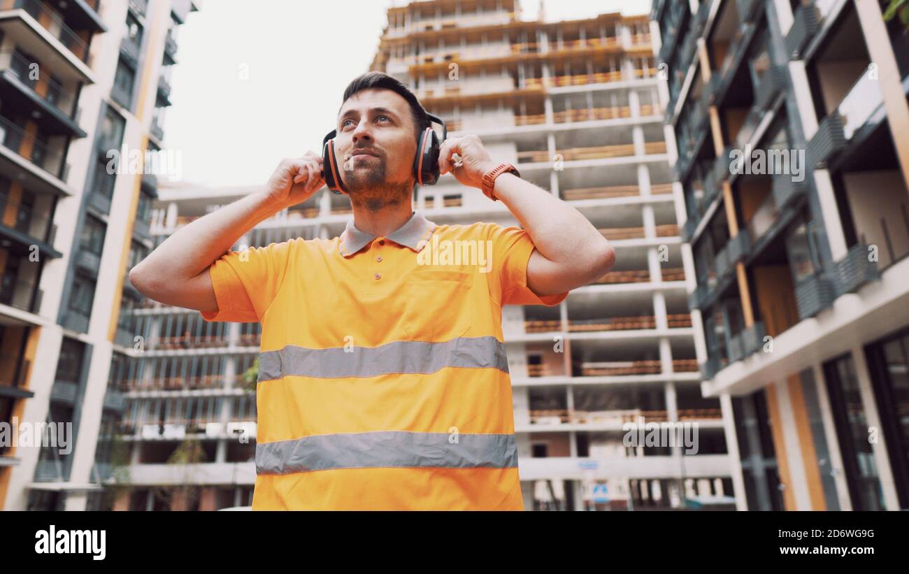 Builder covers his ears, ear muff to protect workers ears. Construction ...