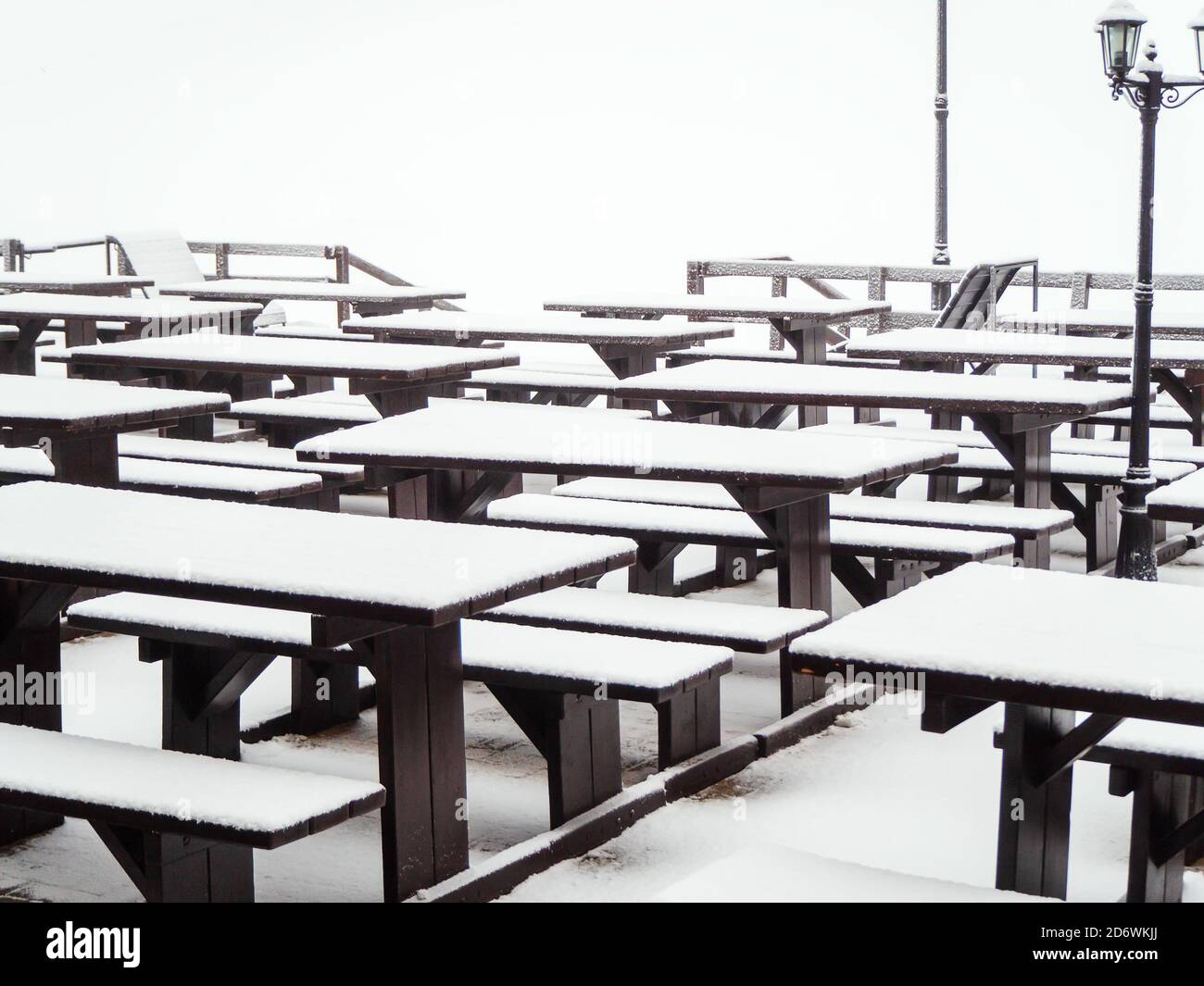 Wooden identical tables with benches covered with snow stand in a row ...