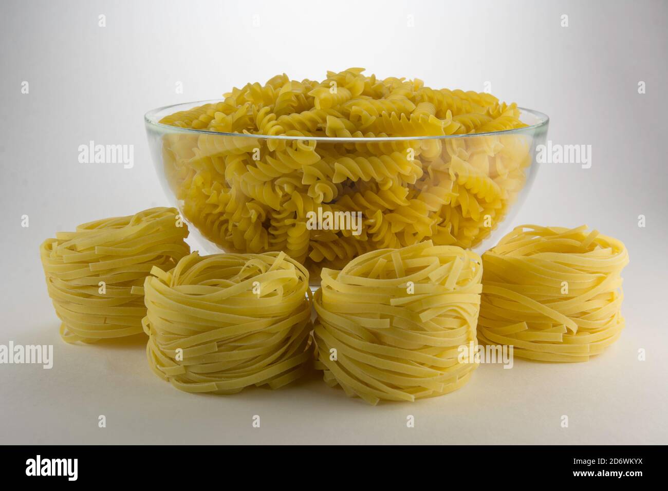 Fusilli in a deep glass plate and fettuccine on a white background ...
