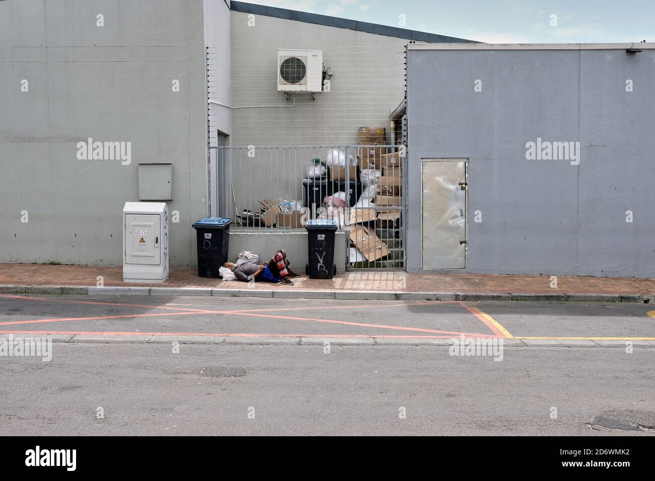 Man sleeping on the side of the street with boxes and garbage stacked ...