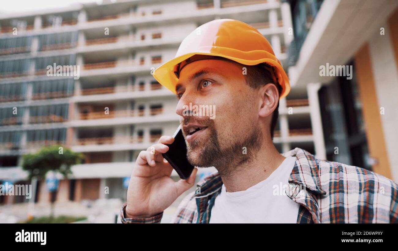 Portrait of young handyman making call while standing at construction ...