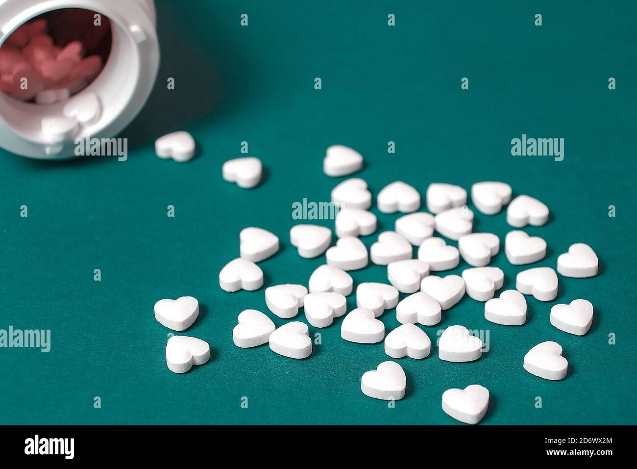 Heart-shaped pills spilled out of the bottle onto the green surface of ...