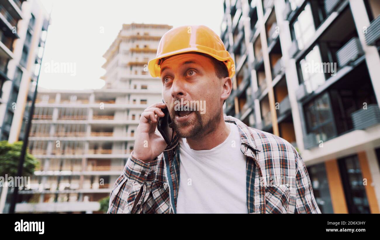 Angry male architect in orange hard hat talks swears on phone at ...