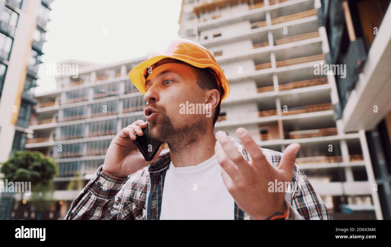 Angry male architect in orange hard hat talks swears on phone at ...