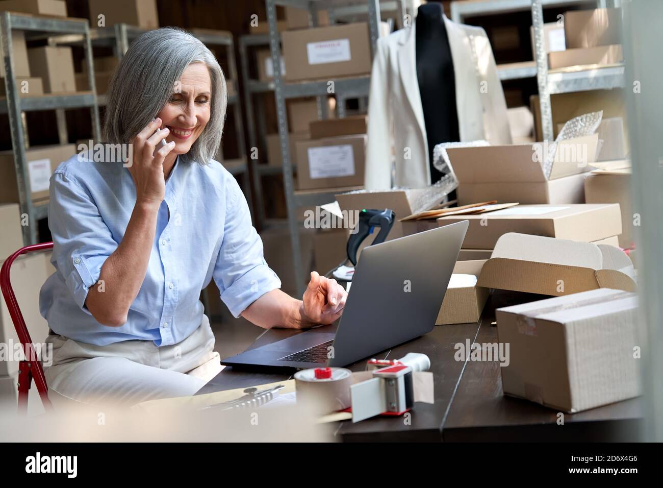 Female dropshipping business owner using laptop talking on phone at ...