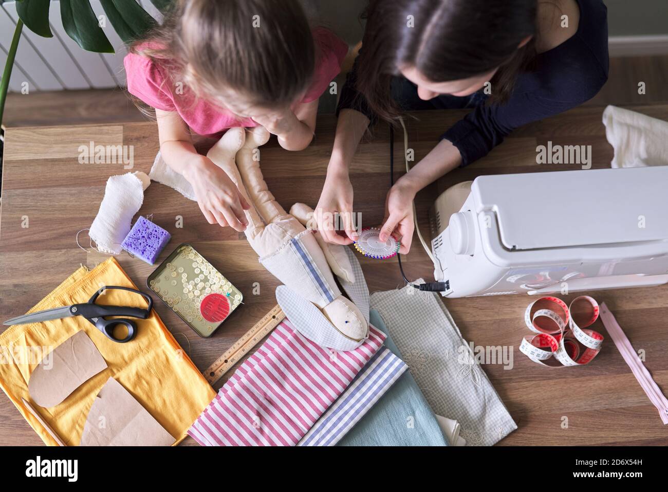 Family, two girls sisters teenager and younger together sewing toy doll ...