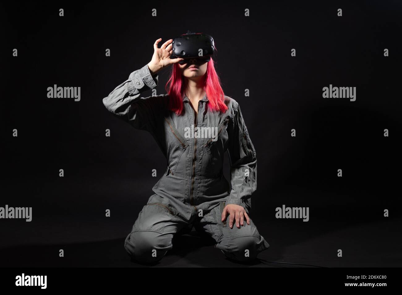Young woman with pink hair and in a jumpsuit uses virtual reality ...