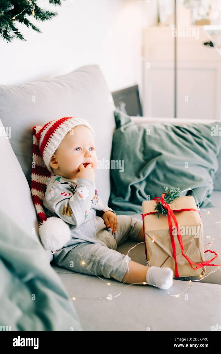 brooding little boy sits in Santa hat and holiday costume on gray sofa ...