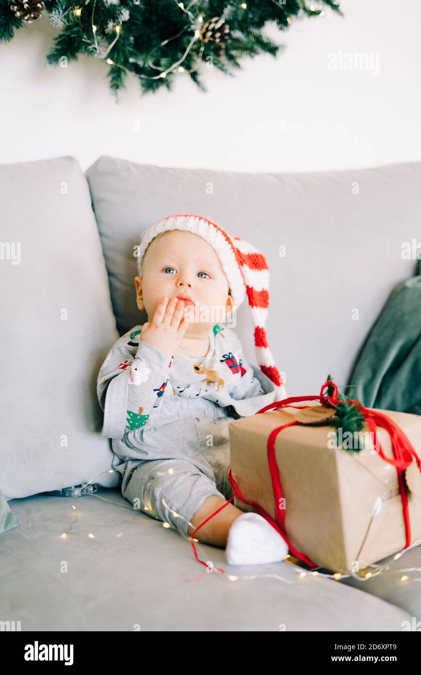brooding little boy sits in Santa hat and holiday costume on gray sofa ...