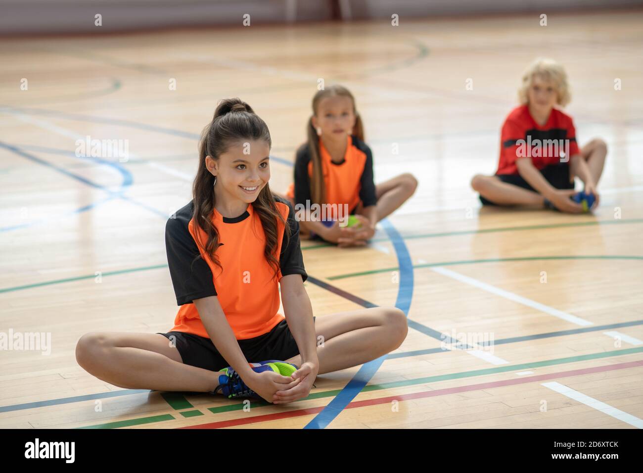 Three kids in bright sportswear stretching legs Stock Photo - Alamy
