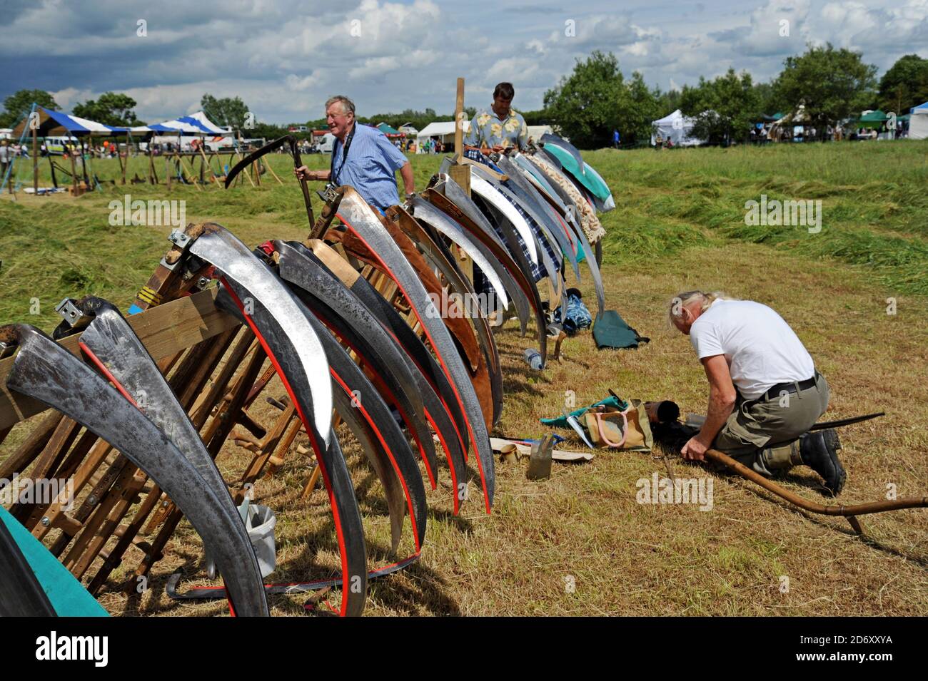 A man sharpens his scythe next to a rack of competition scythes at the ...