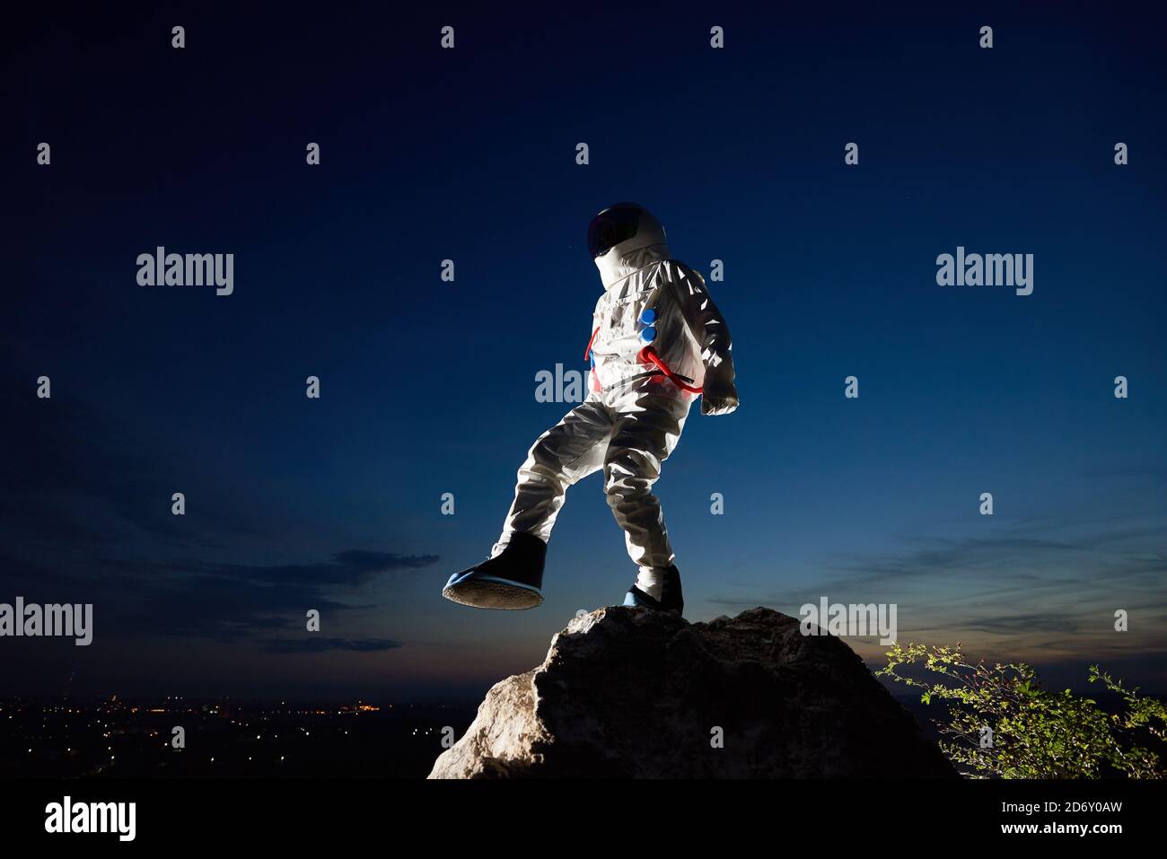 Full length of astronaut standing on one leg on top of mountain with ...