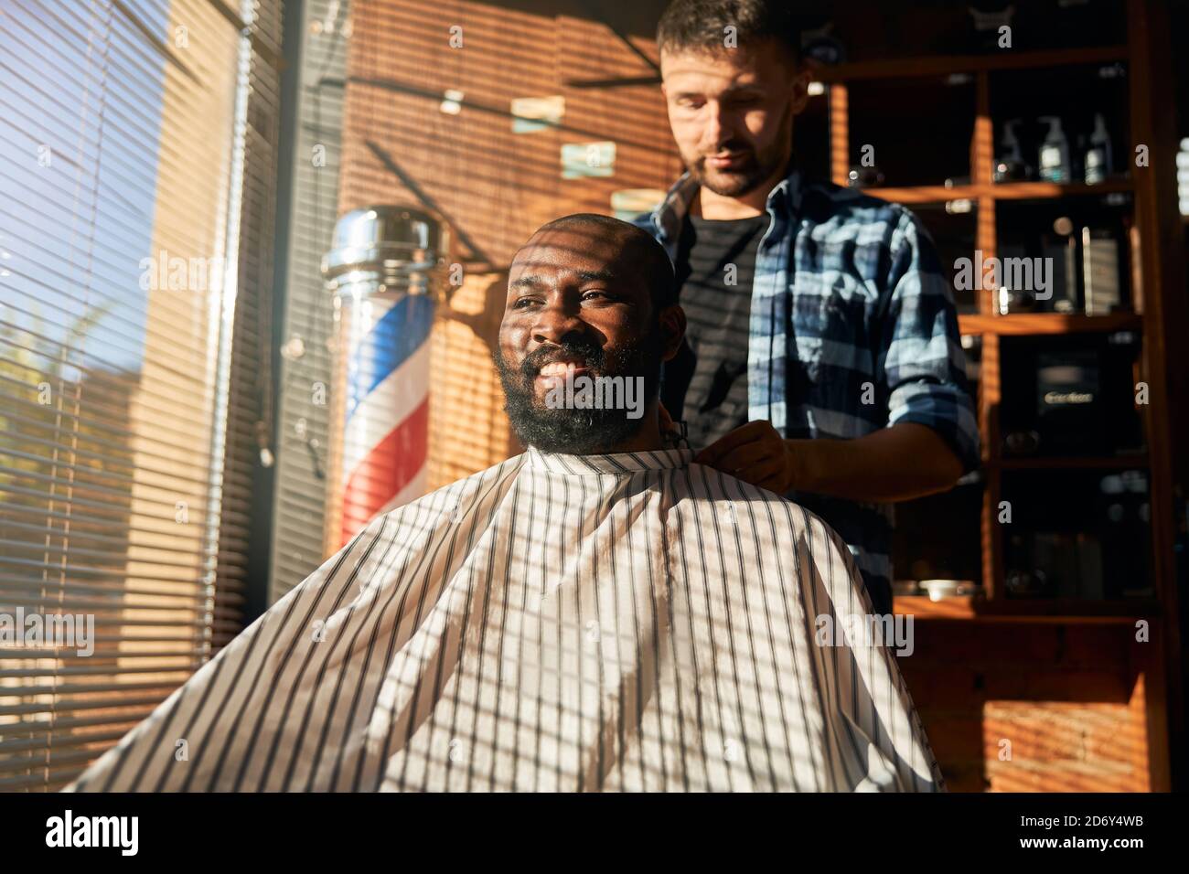 Male barber putting cape on client at barbershop Stock Photo - Alamy
