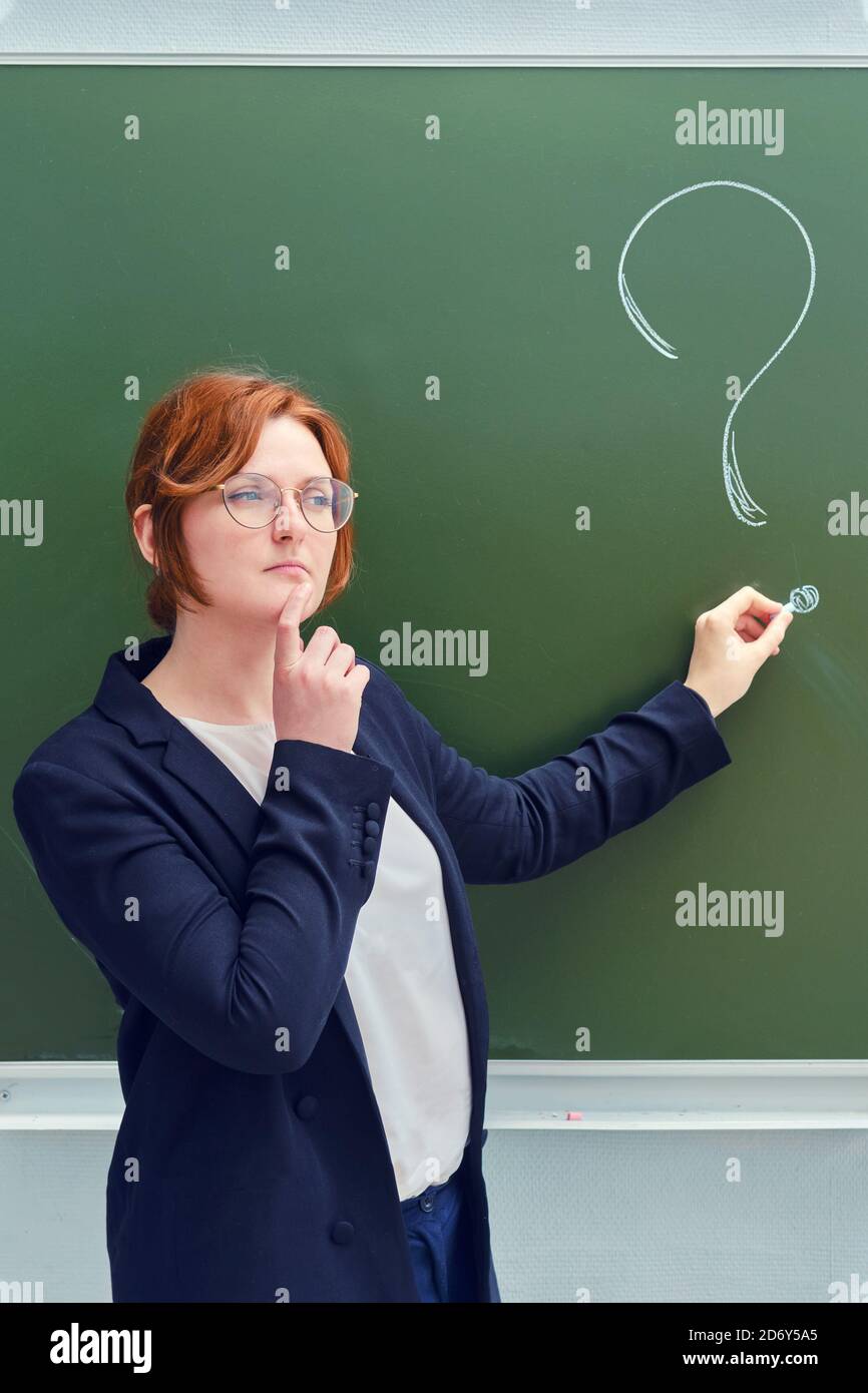 Woman teacher with a sad face and a question mark on a blackboard ...