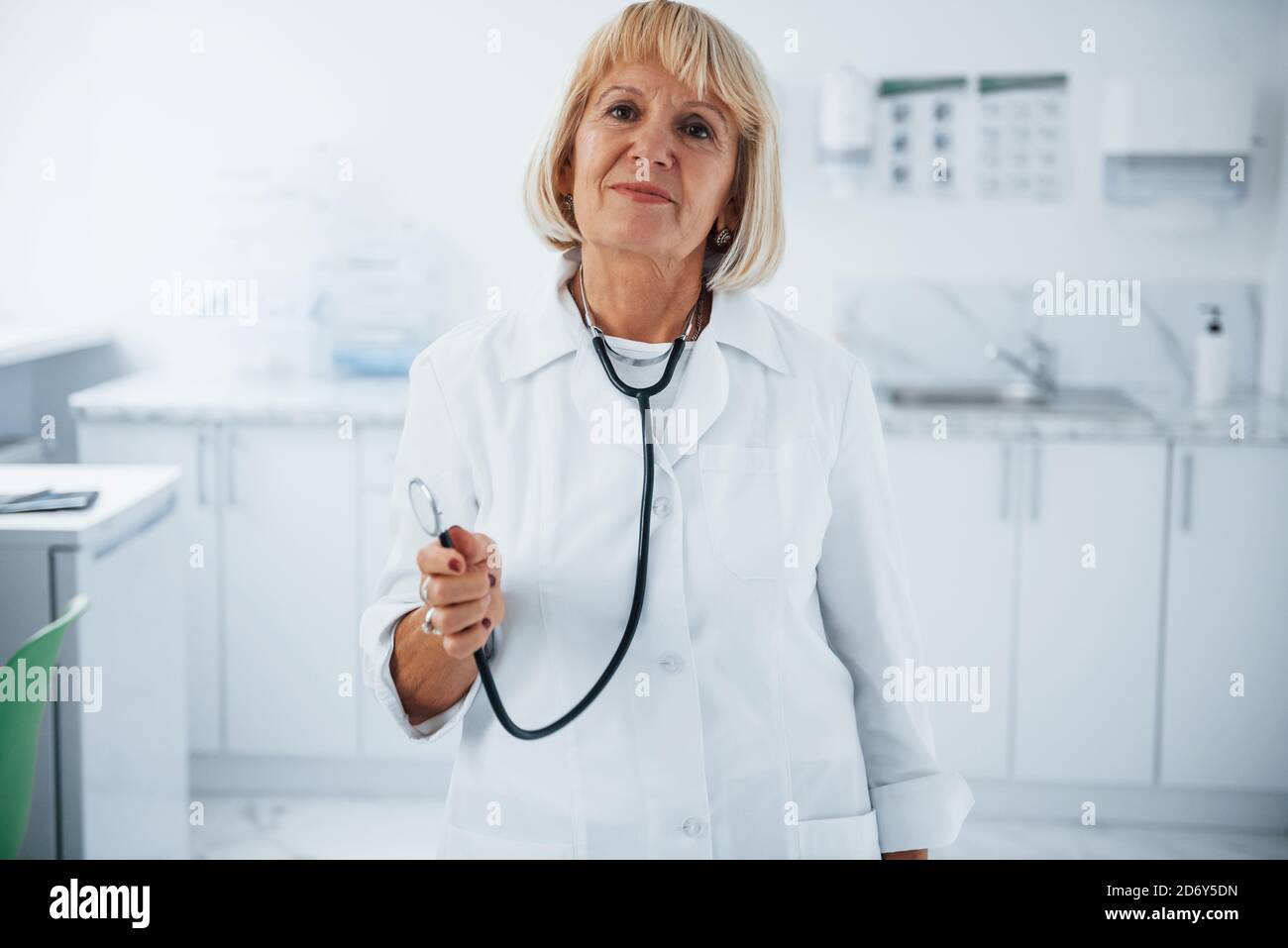 Holds stethoscope in hand. Portrait of senior doctor in white uniform ...