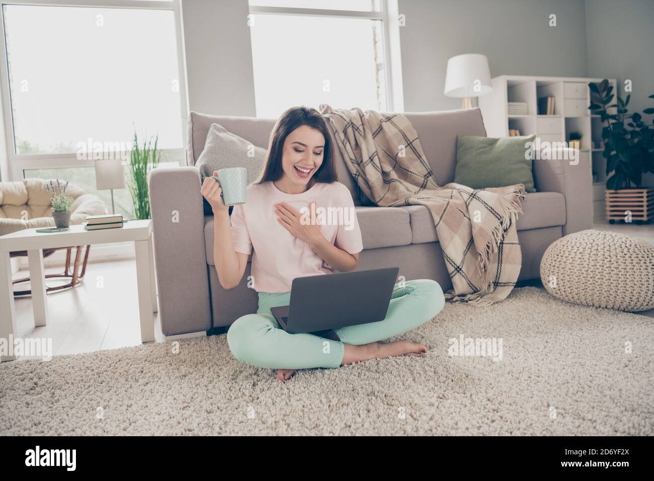 Photo portrait of woman sitting on floor rug with laptop holding mug ...