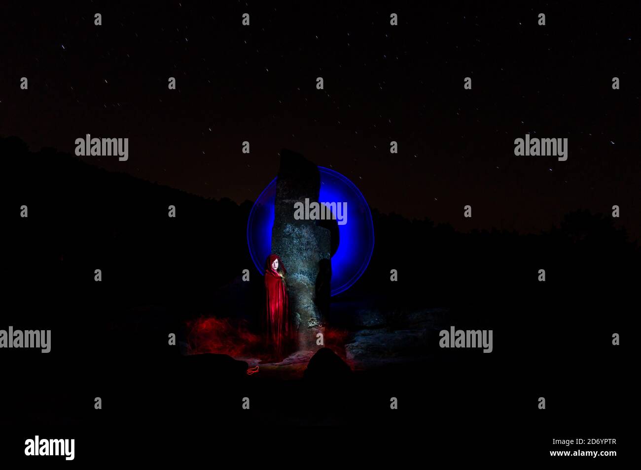 A mysterious woman with a full-length cloak standing next to a stone ...