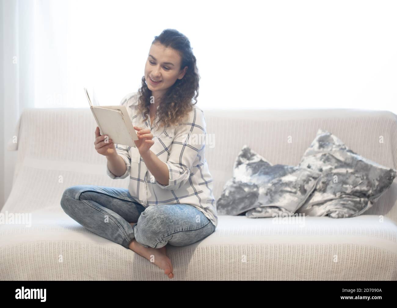 Beautiful girl reading a book sitting on the sofa in a bright room. the ...