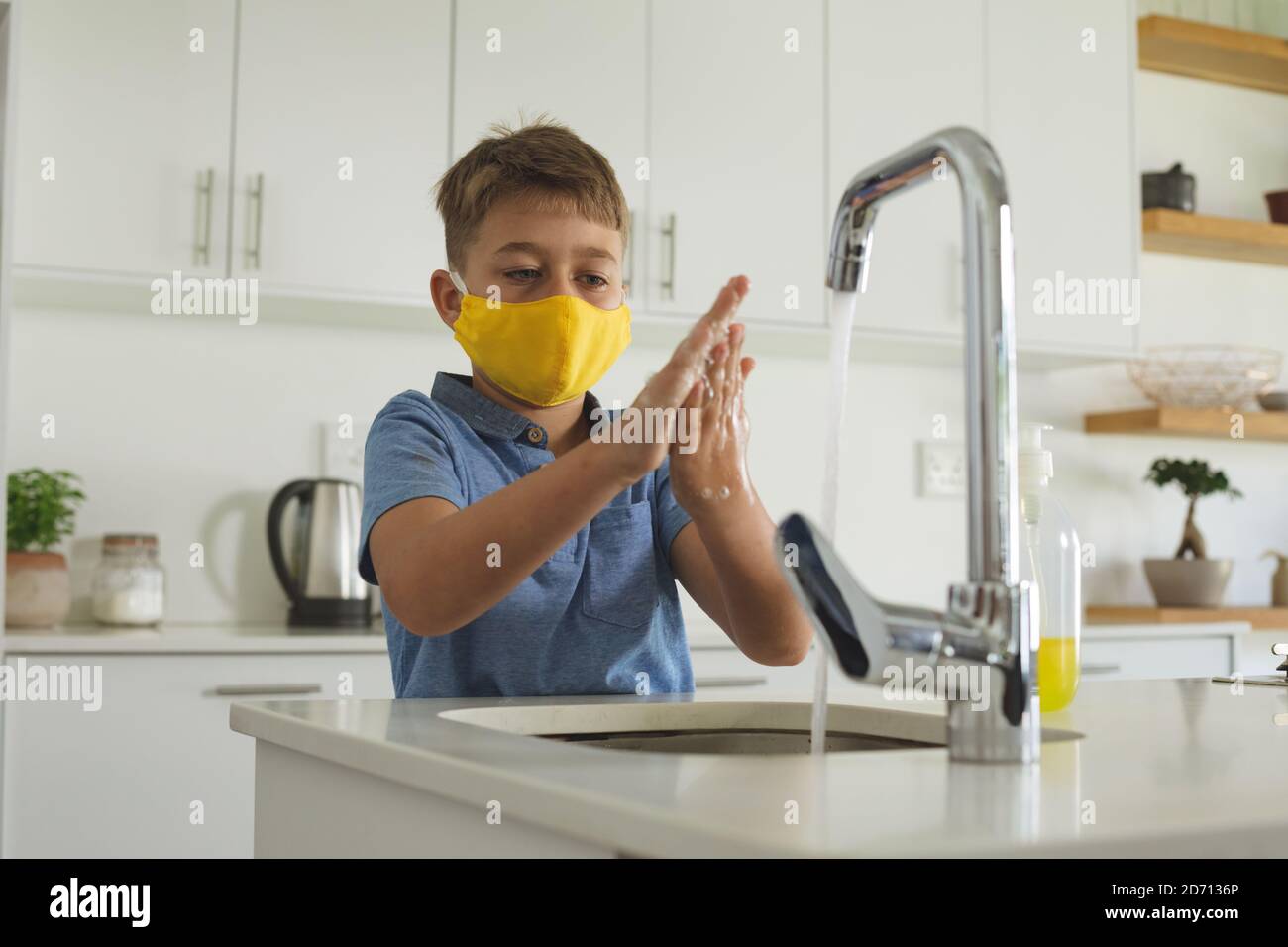 Caucasian boy spending time at home, in kitchen washing his hands ...