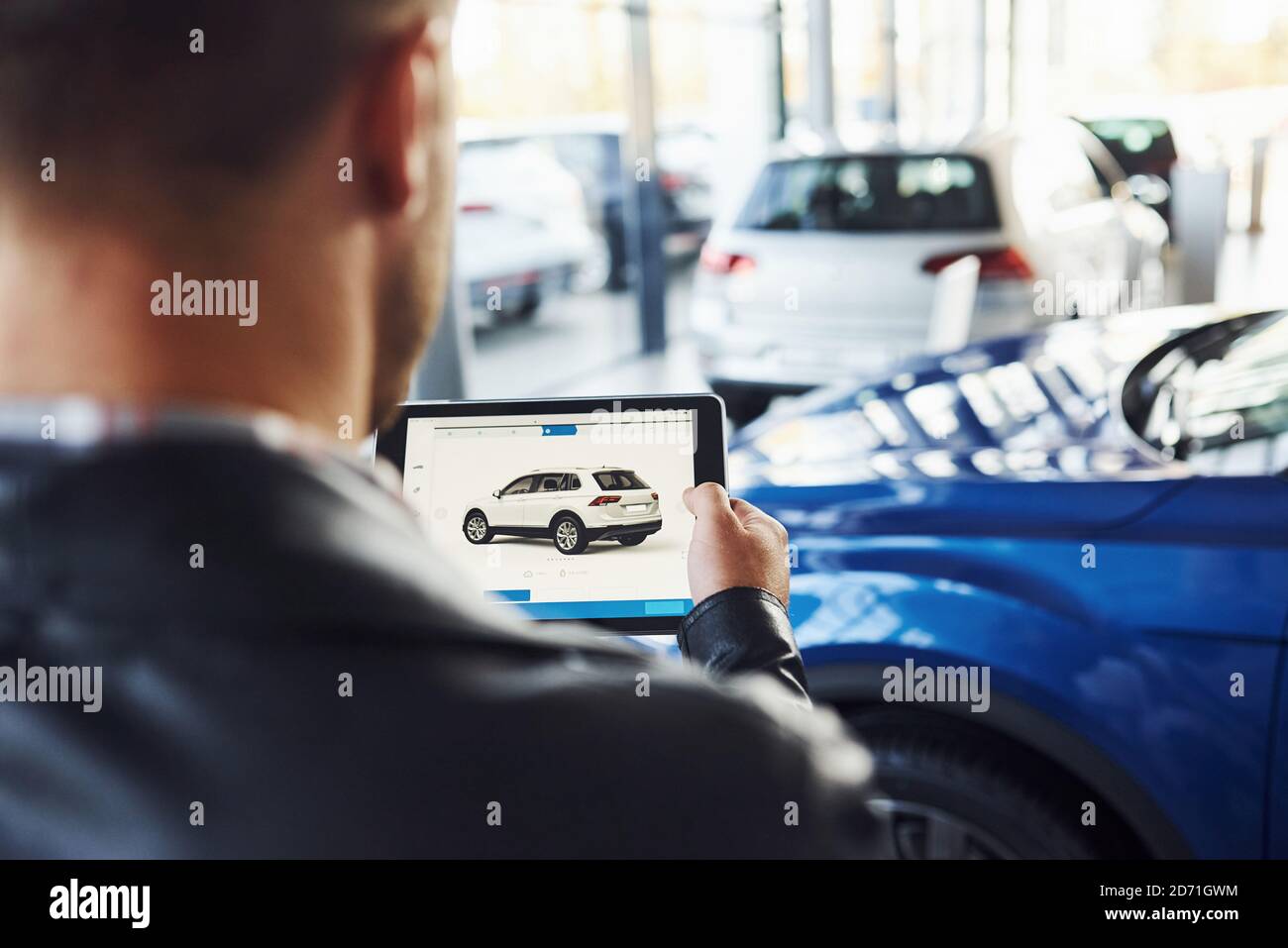 Man stands inside car salon with tablet in hands and looks at the ...