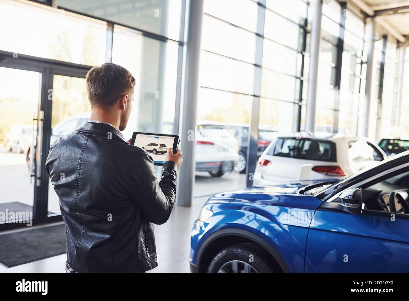 Man stands inside car salon with tablet in hands and looks at the ...