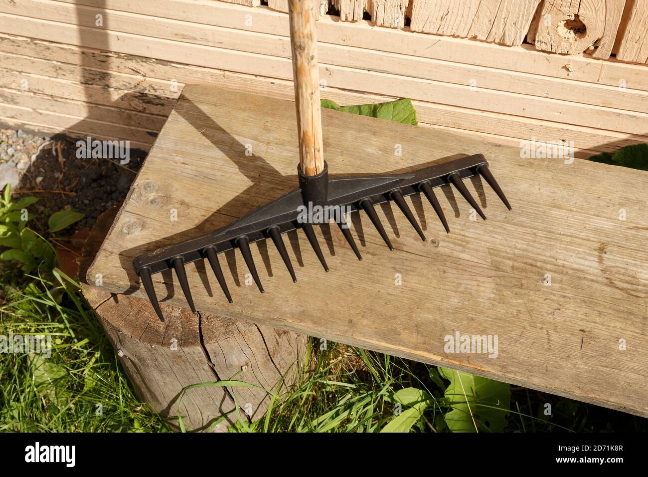 A black rake stands on a wooden bench near the wall of the house Stock ...