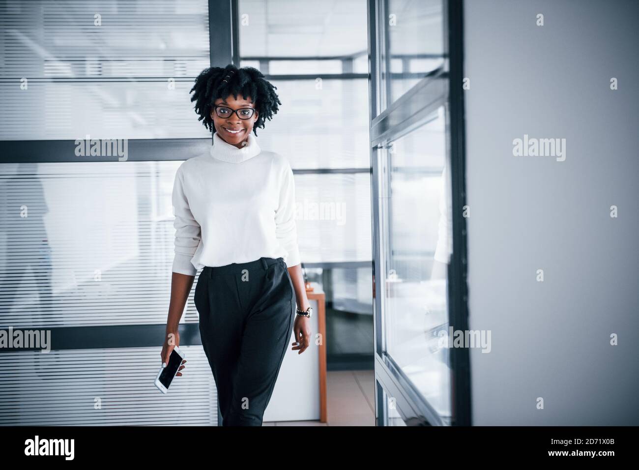 Young african american woman in glasses stands indoors in the office ...