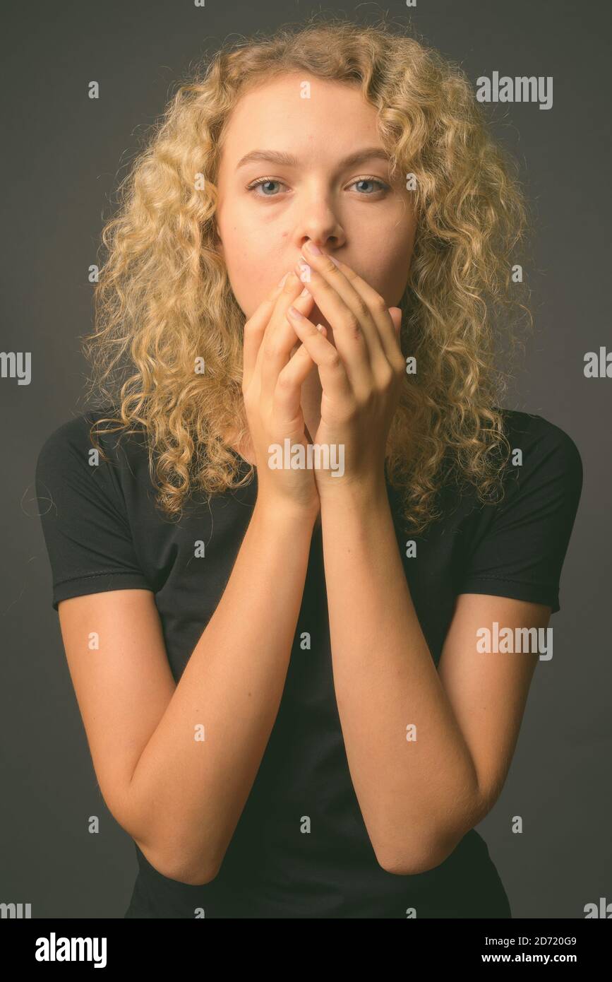 Young beautiful woman with curly blond hair against gray background ...