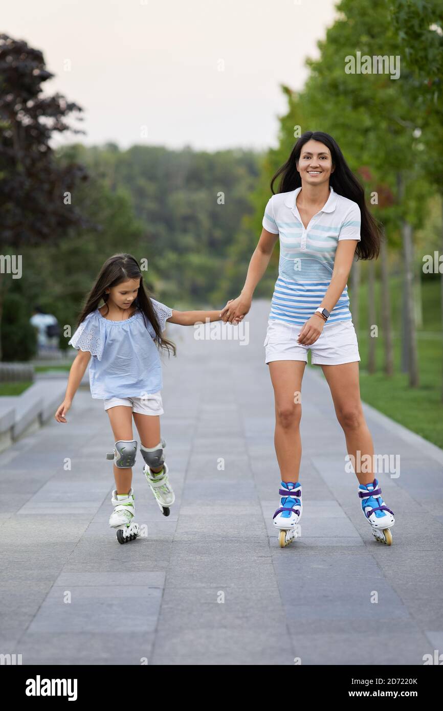 Young mother and her little daughter rollerskating in summer park ...