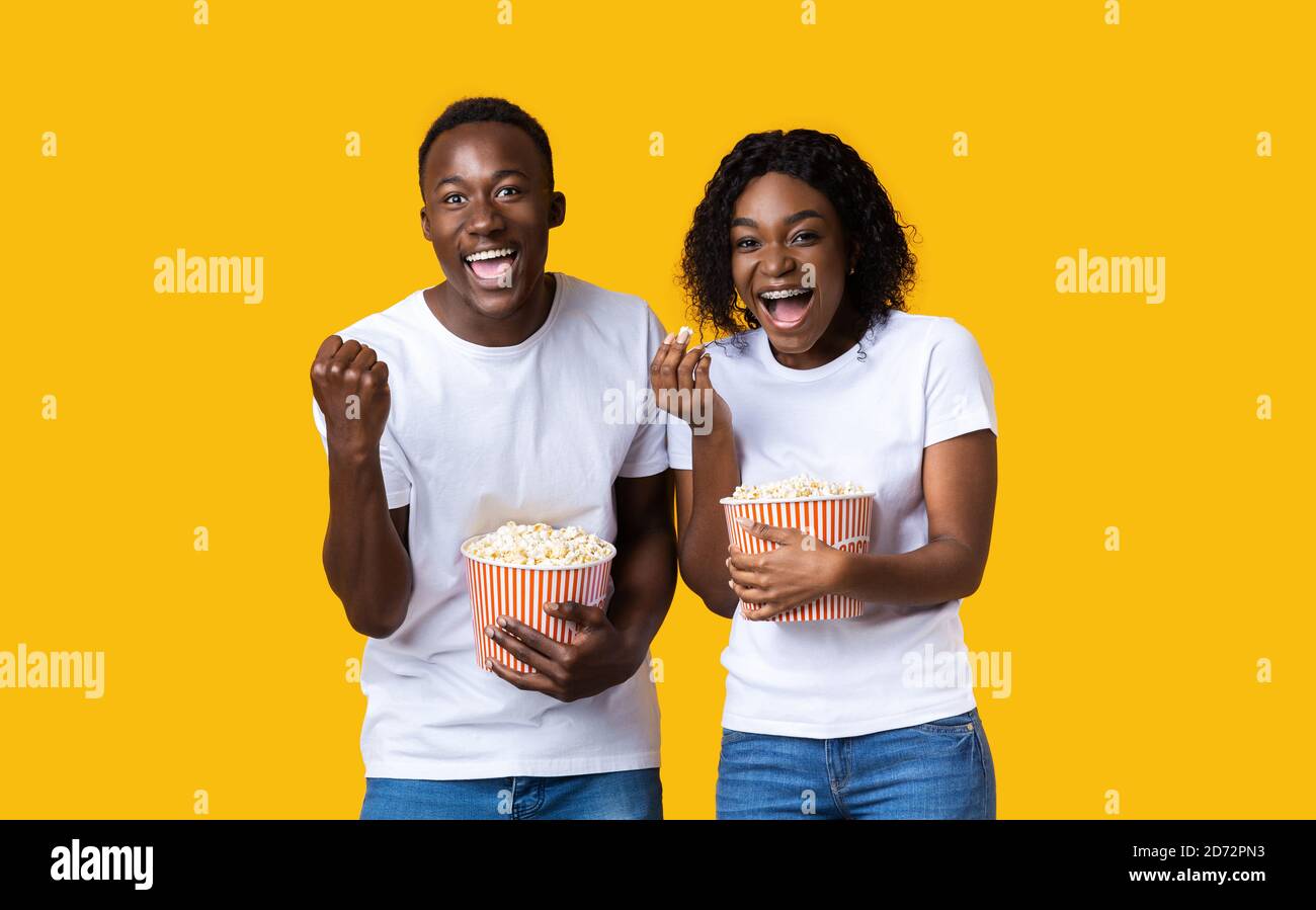 Excited black man and woman eating popcorn on yellow background Stock ...
