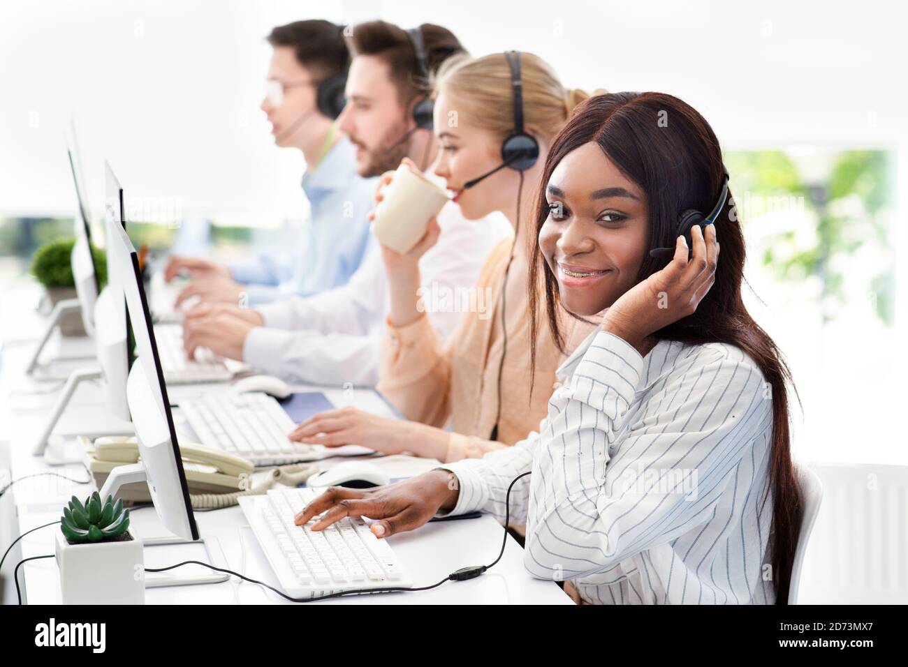 Group of call centre representatives with headsets working on computers ...