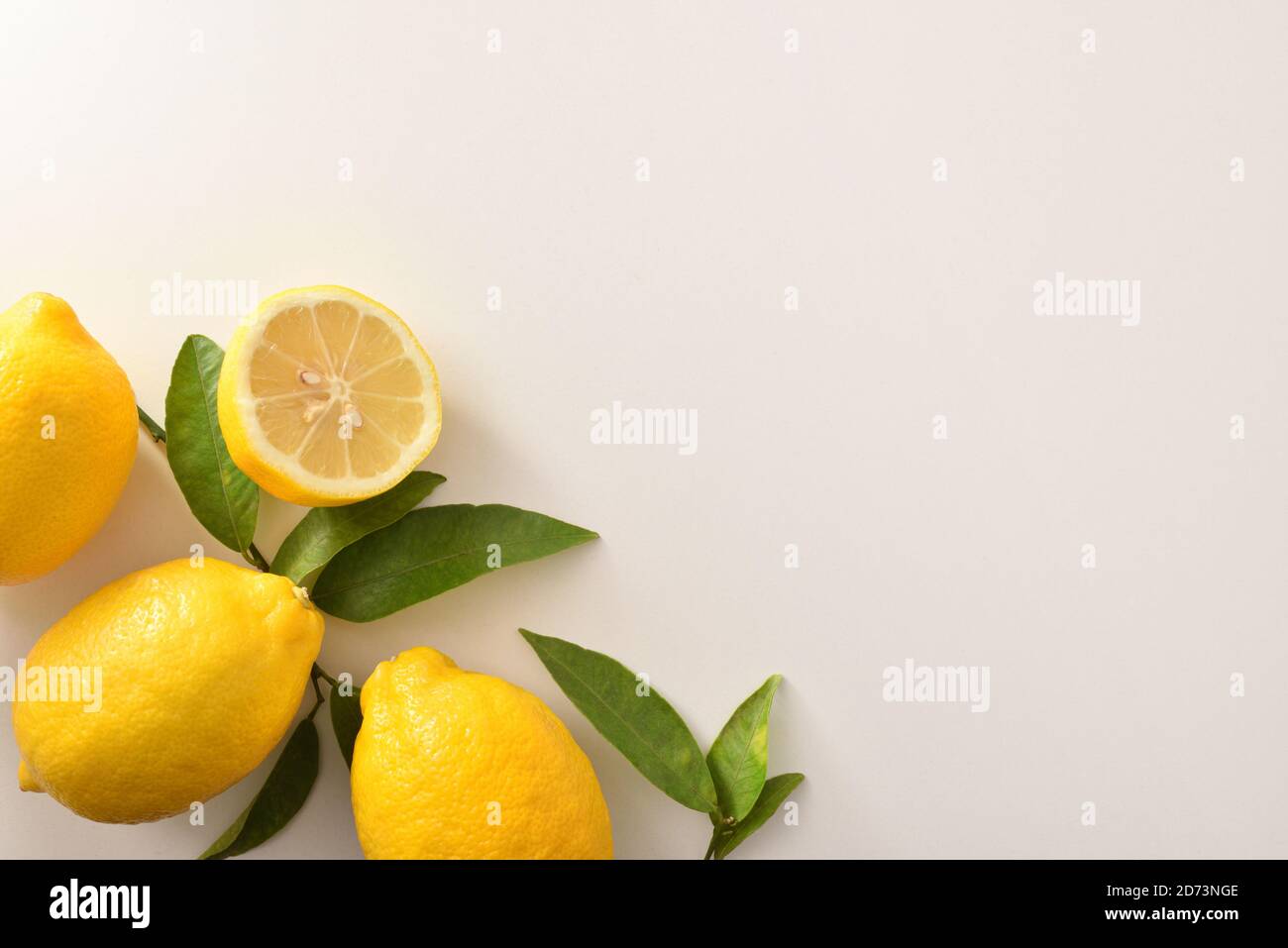 Group of lemons with leaves and section of a lemon on white table. Top ...